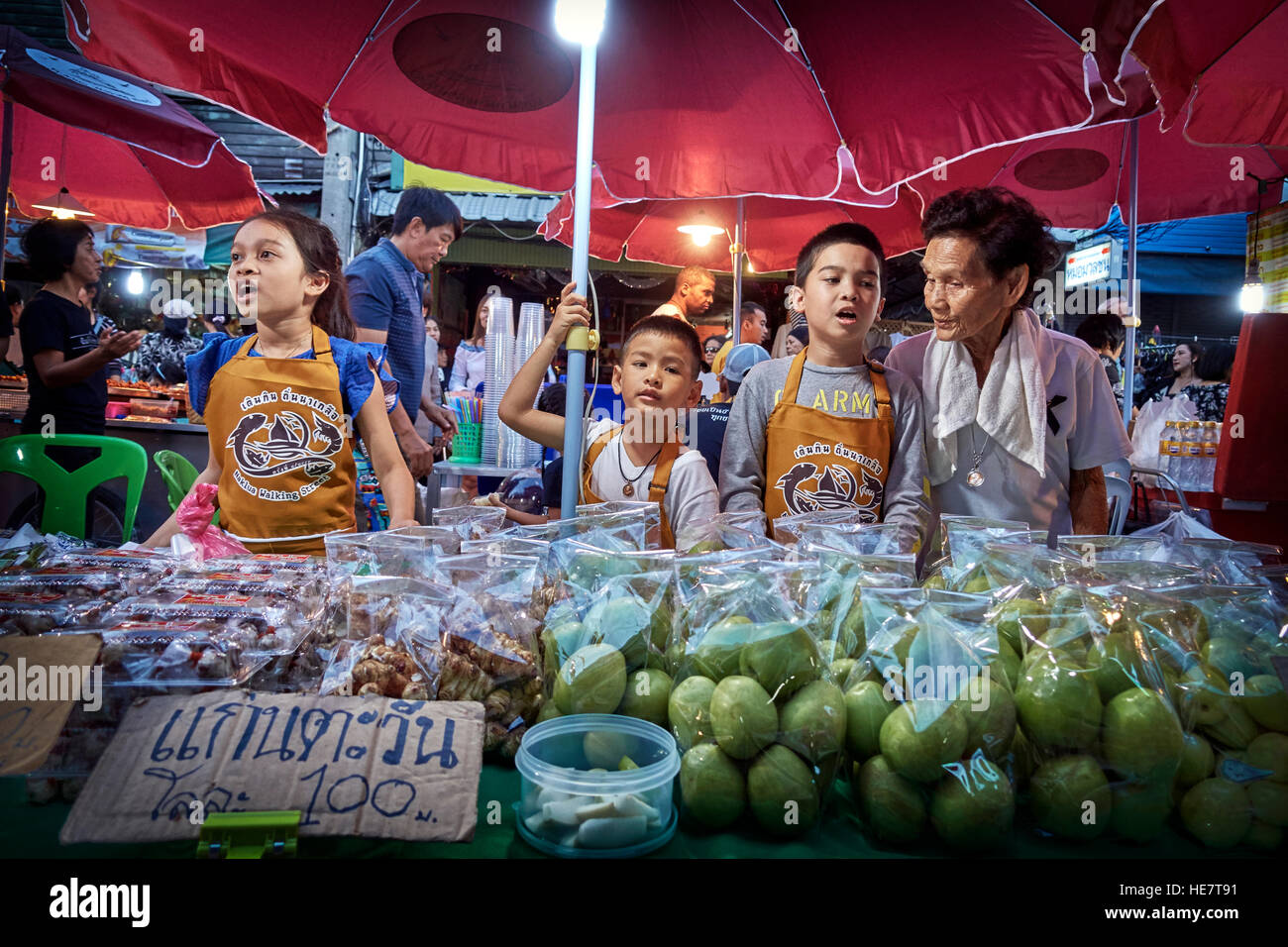 Young Thai children helping out on the family food stall at a nighttime ...