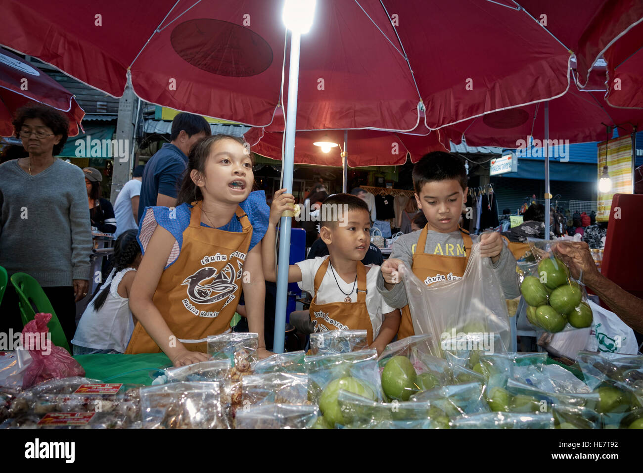 Young Thai children helping out on the family food stall at a nighttime ...