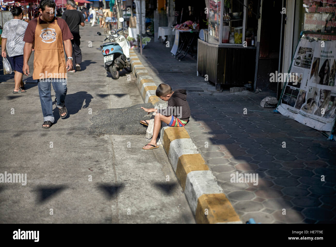 Lonely child playing alone outside in a Thailand street. S. E. Asia ...