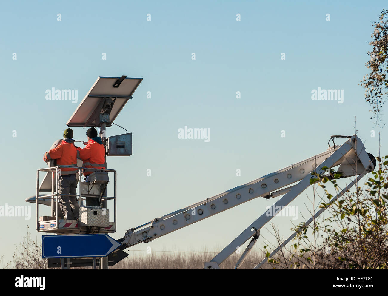 Workers in lift bucket during the maintenance of streetlight powered by ...