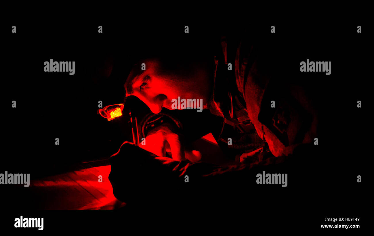 A soldier plots points on a map under a tarp during the rain while ...