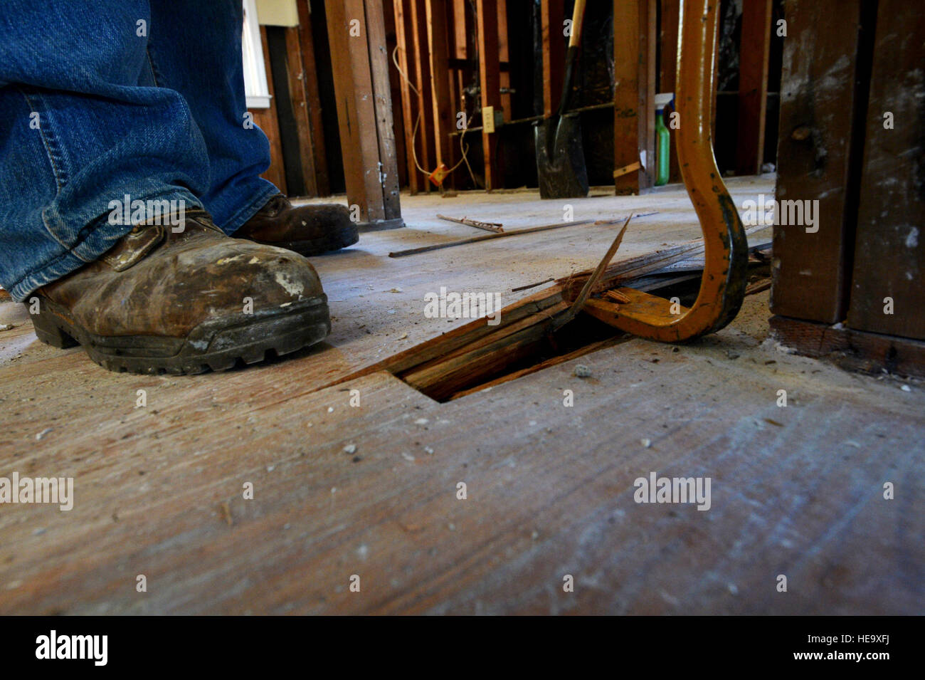 A disaster relief volunteer uses a crowbar to remove wood floors from a ...