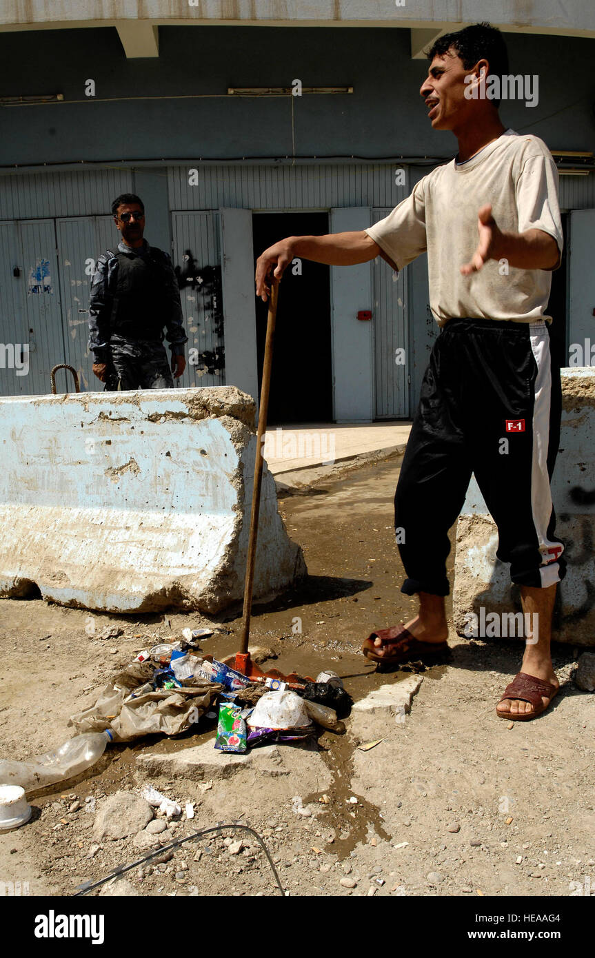 An off duty Iraqi police officer sweeps up trash from the street in the ...