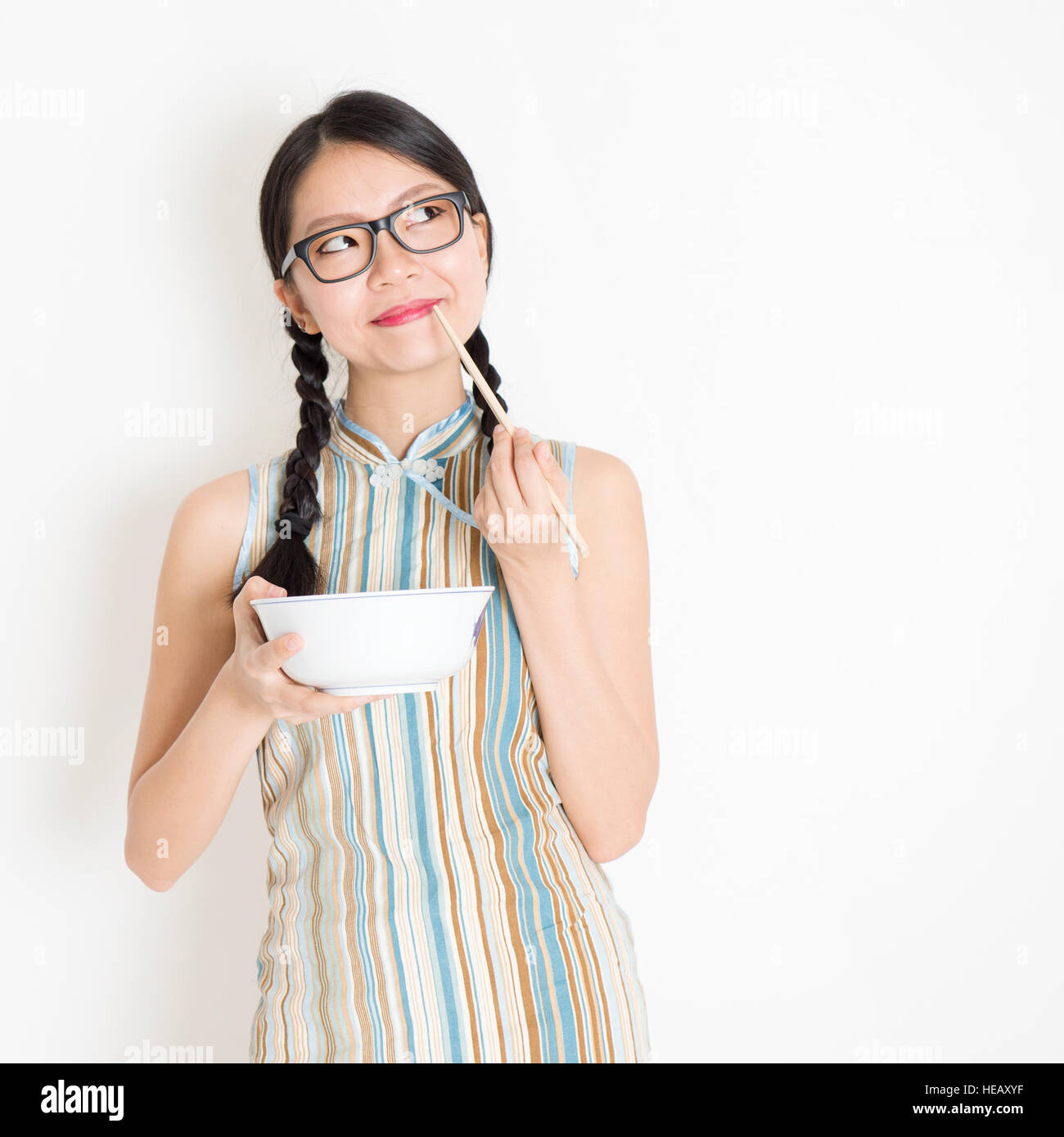 Portrait of young Asian woman in traditional qipao dress eating with ...