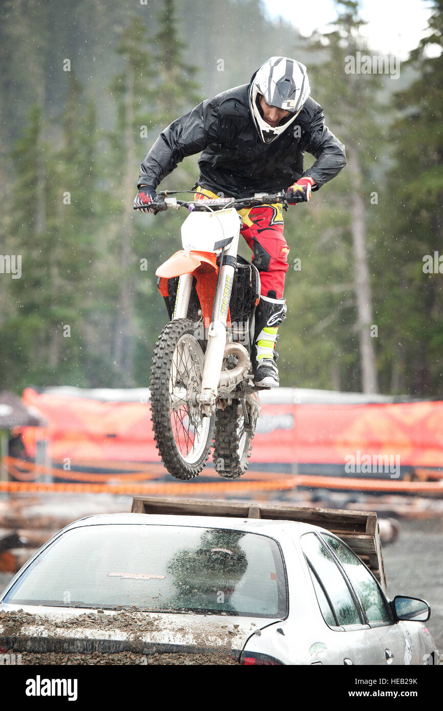 An enduro rider rides his motorcross bike over a wrecked car at the ...