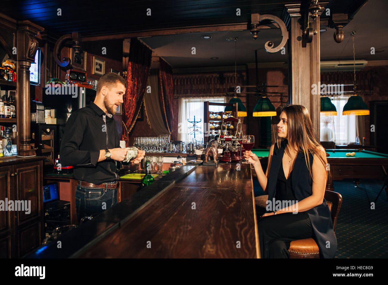 beautiful young woman sitting at the bar talking with the bartender ...