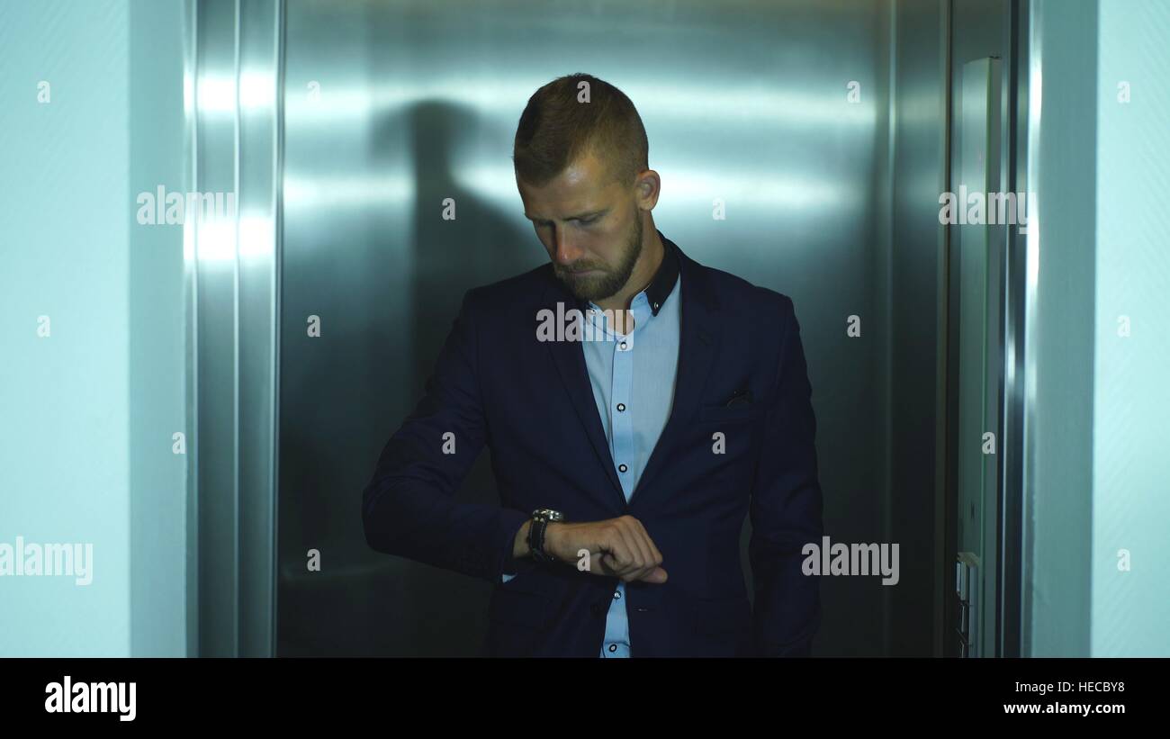 young and successful businessman exits the Elevator looks at his watch ...