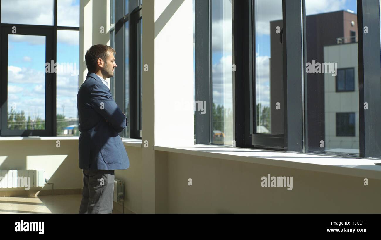 a successful businessman looks out the window and ponders the business ...