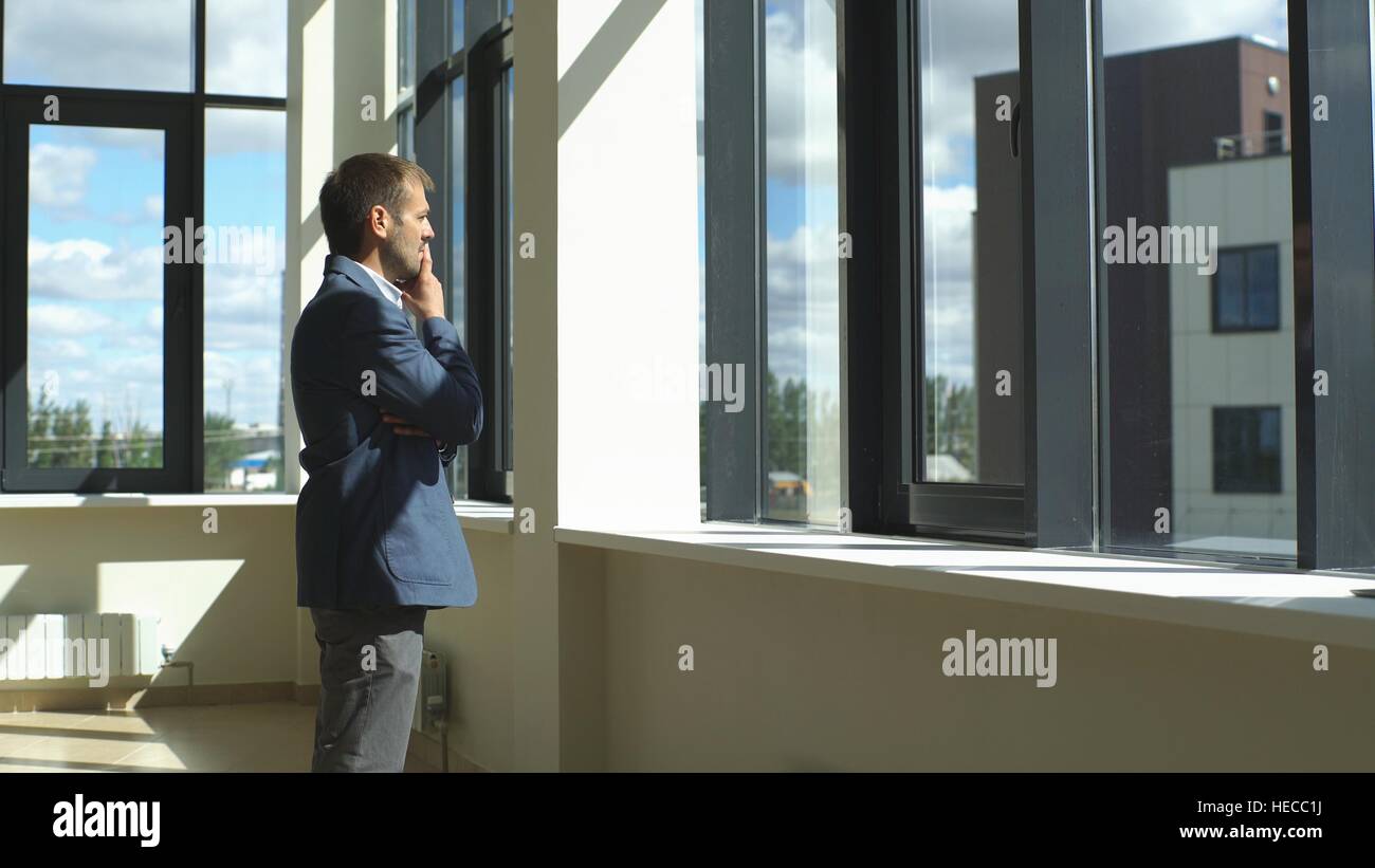 a successful businessman looks out the window and ponders the business ...