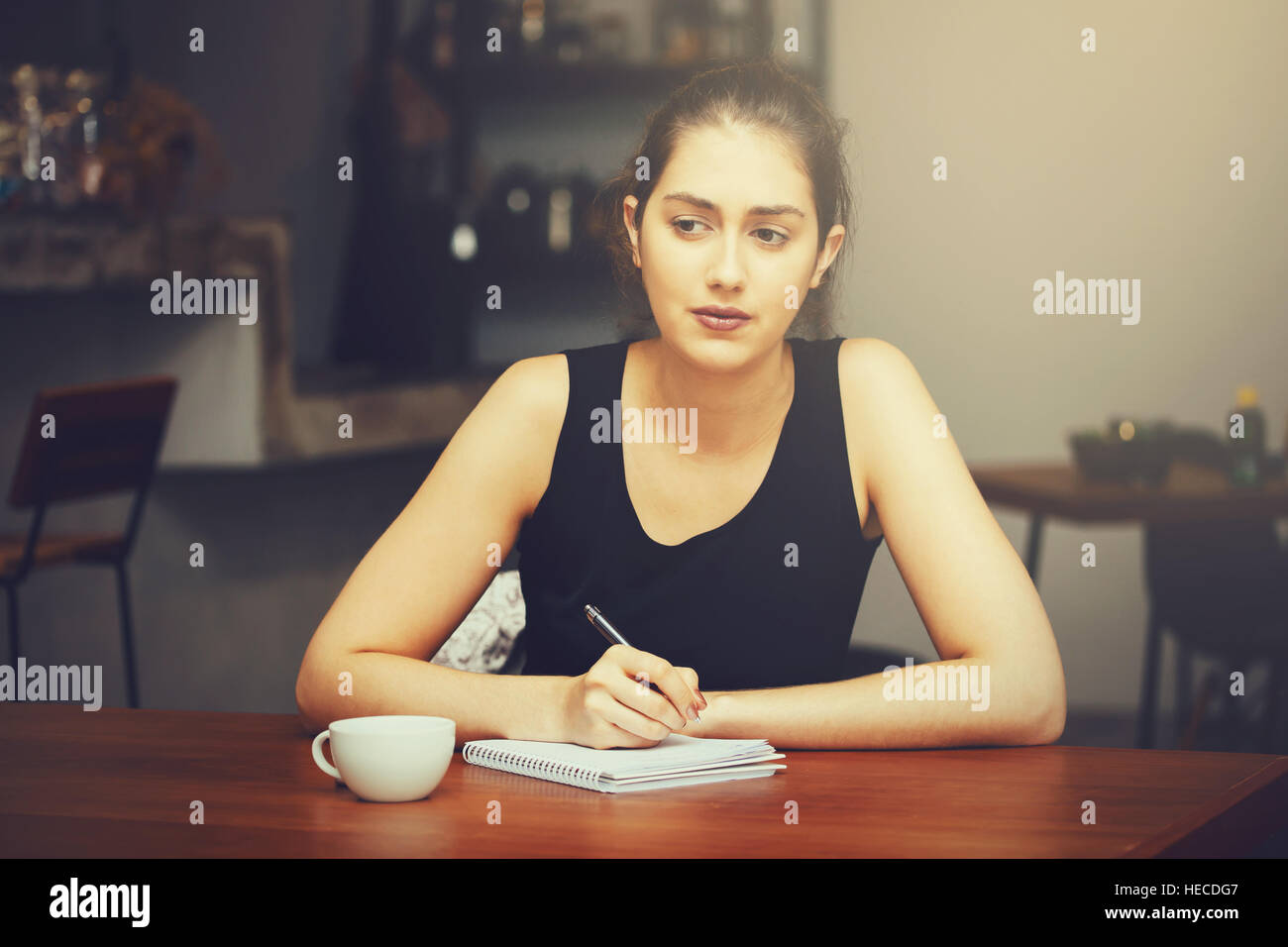 Young Caucasian woman thinking and writing something on a notebook in ...
