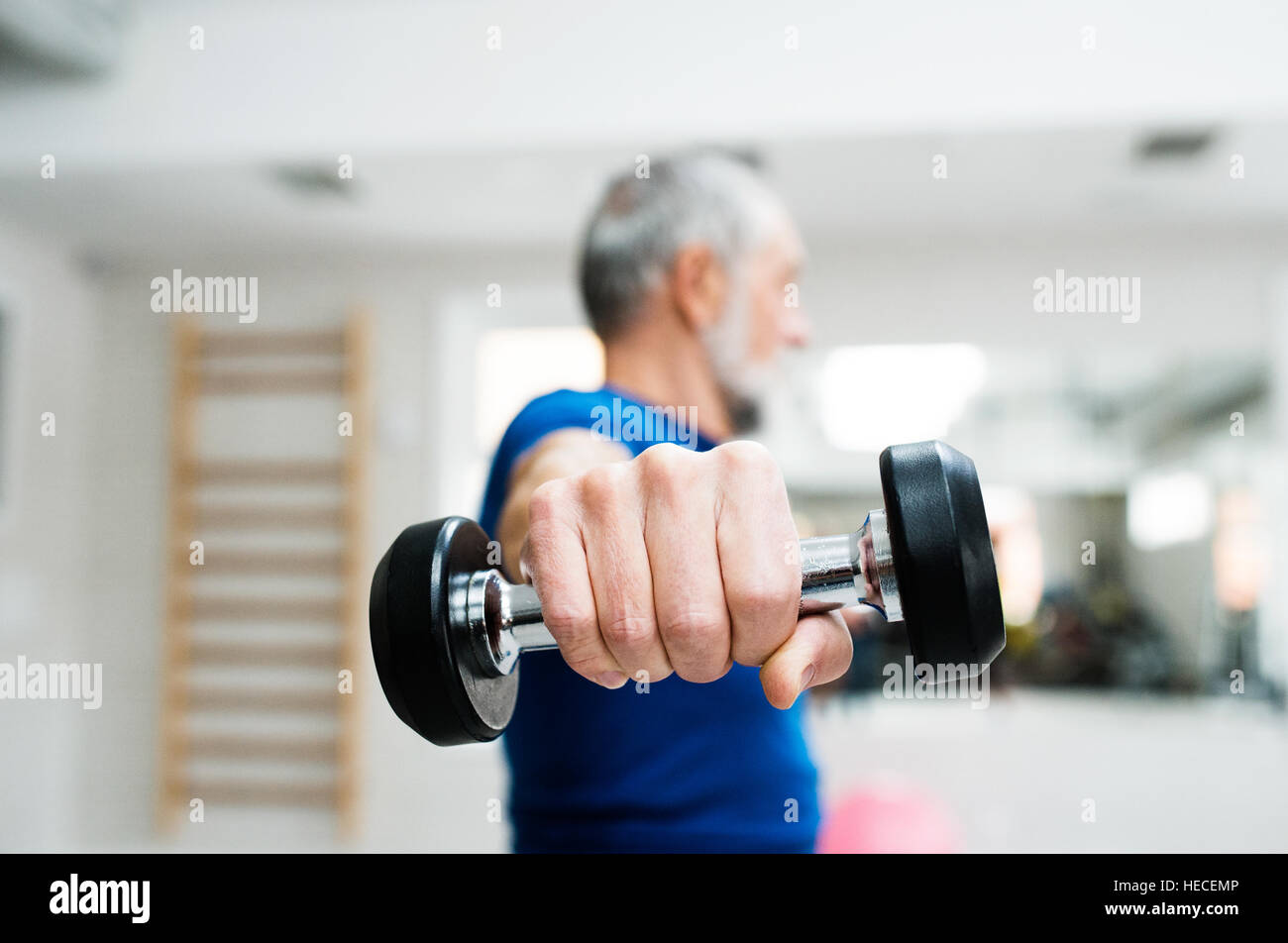 Senior man in sports clothing in gym working out with weights. Close up ...