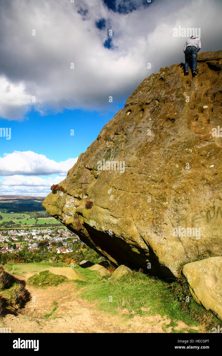 Man climbing a large boulder stone to enjoy views across Wharfedale ...