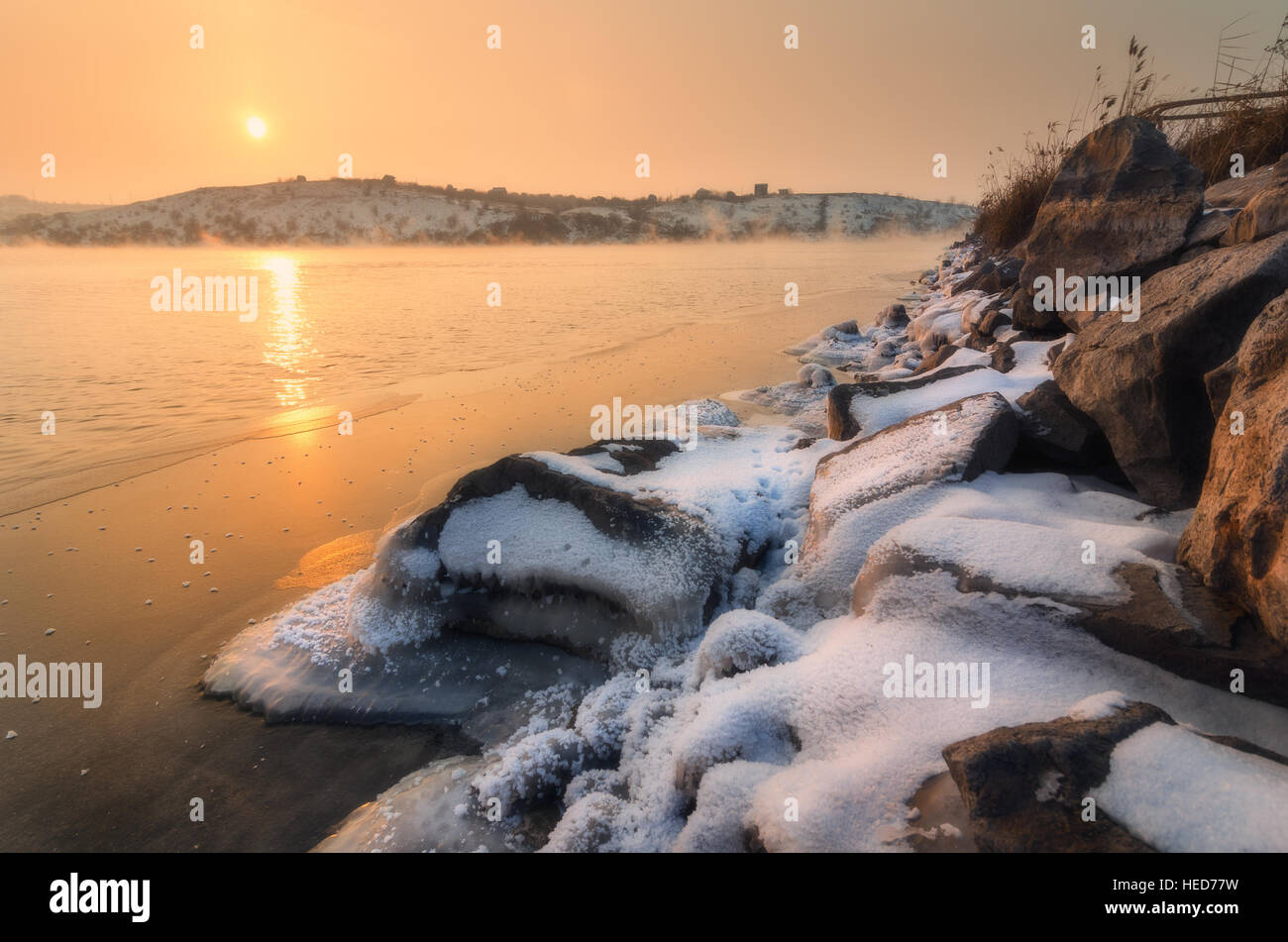 Winter landscape with snowy stones at the beautiful river at sunset ...