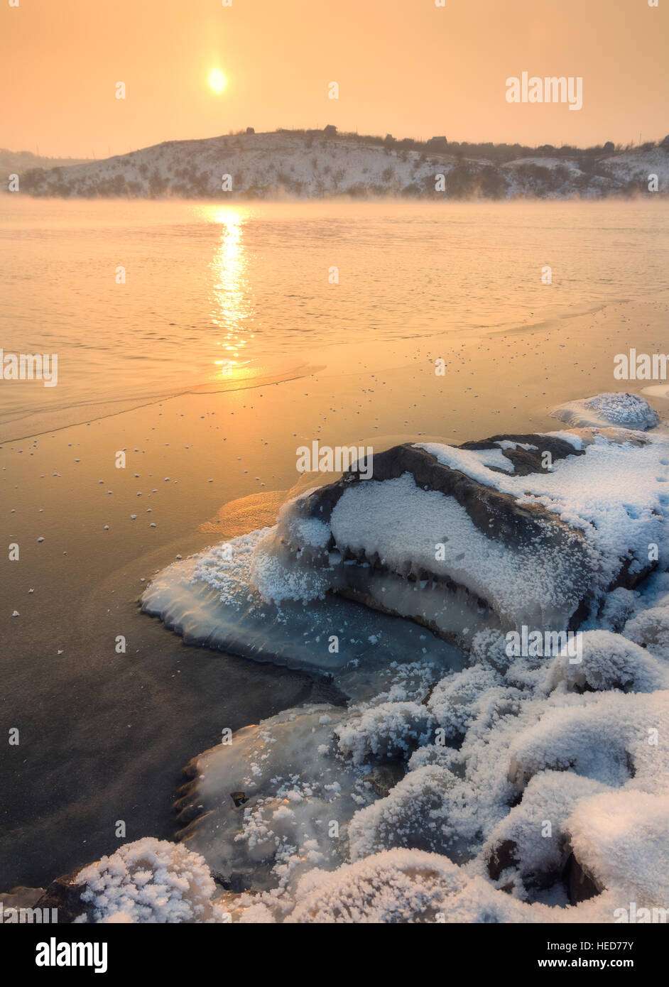 Winter landscape with snowy stones at the beautiful river at sunset ...