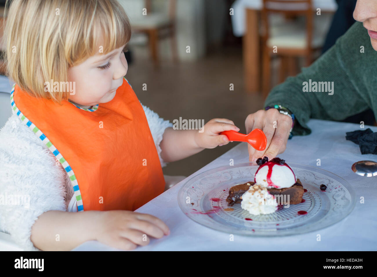 two years old child with orange plastic spoon sharing with woman a ...