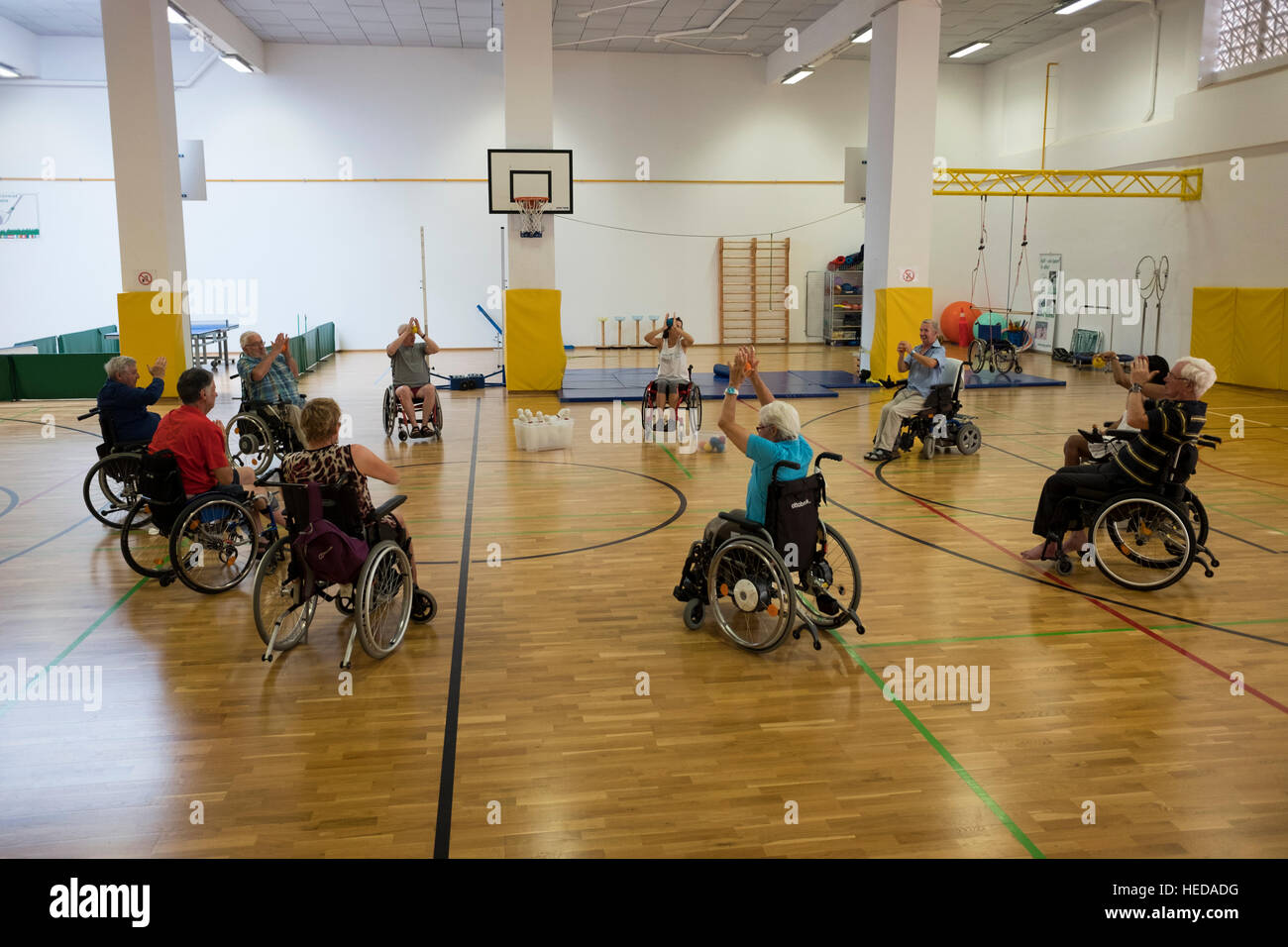 An exercise class in a sports hall for wheelchair users lead by a woman ...