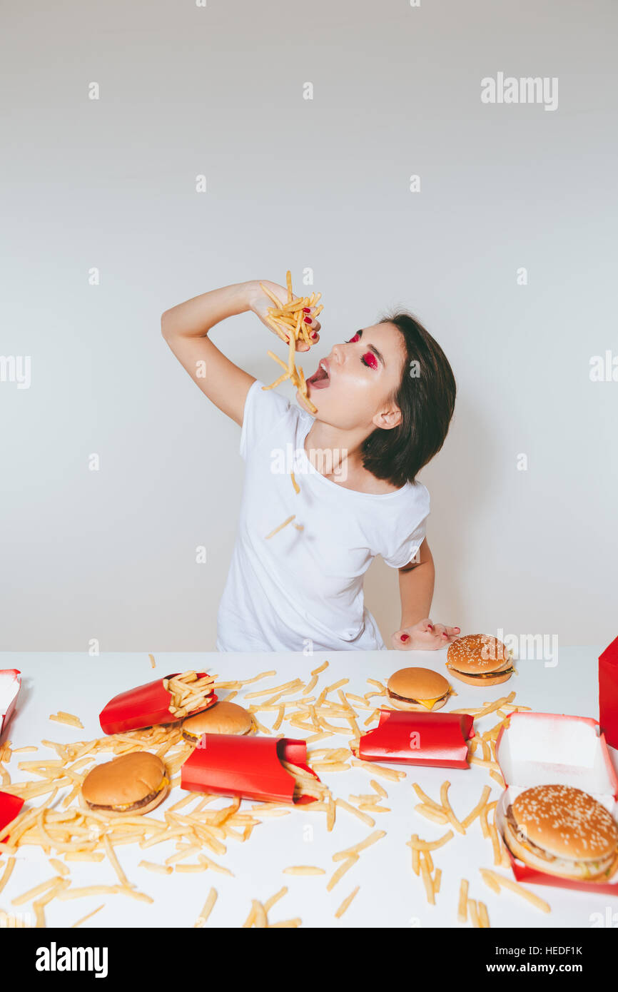 Attractive young woman eating french fries at the table with fast food ...
