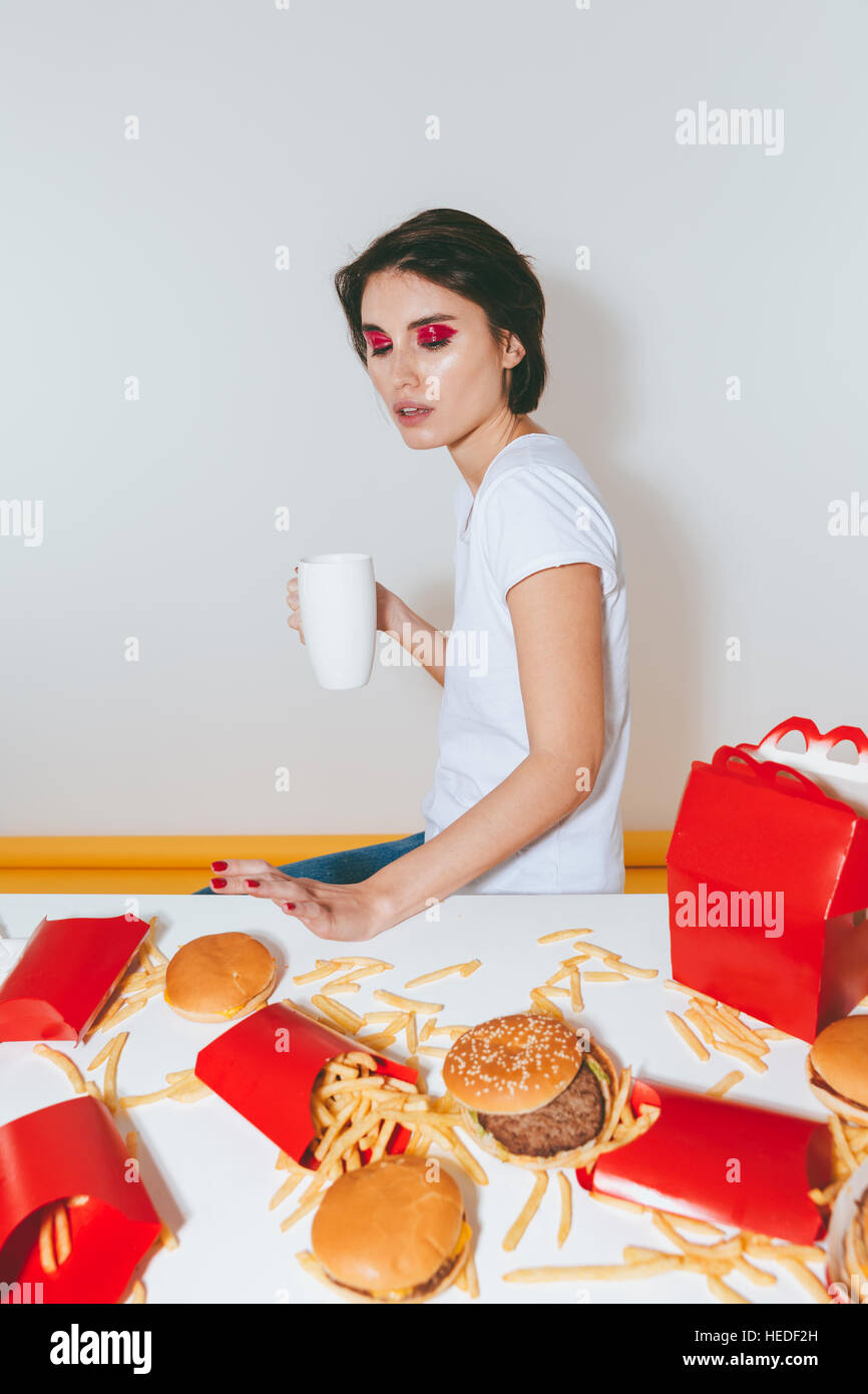Lovely young woman with white mug sitting and refusing from fast food ...
