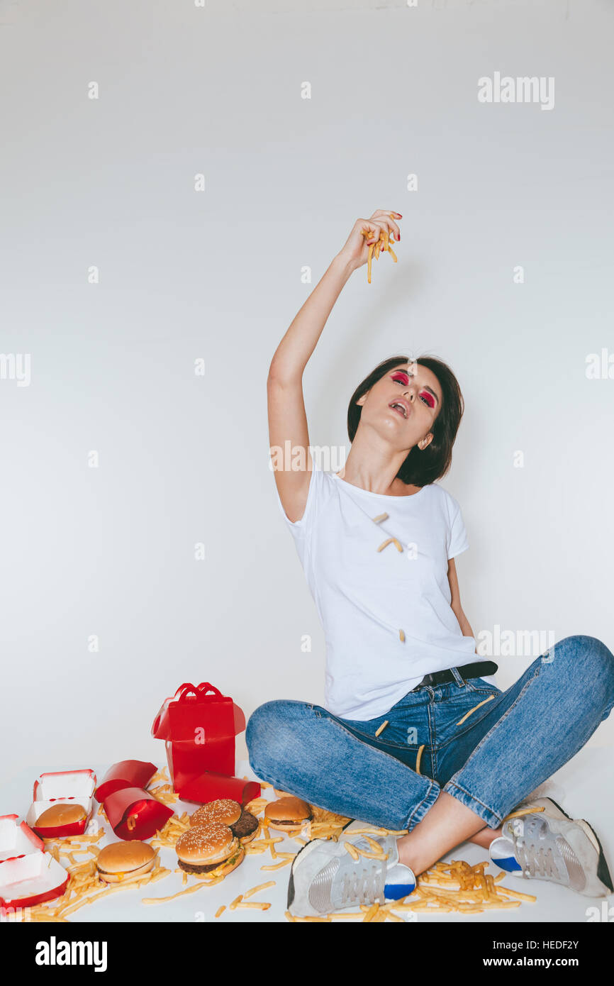 Pretty young woman eating french fries and having fun over white ...