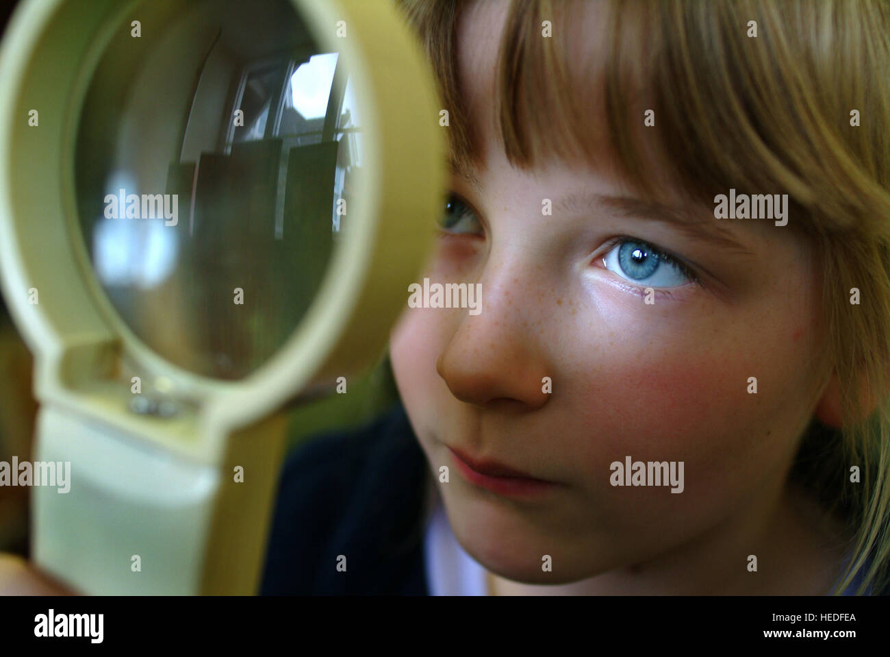 A primary aged schoolgirl peering through a large magnifying glass.a UK ...