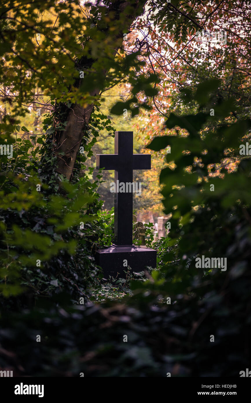 Cross-shaped tombstone surrounded by bushes at the Highgate Cemetery ...