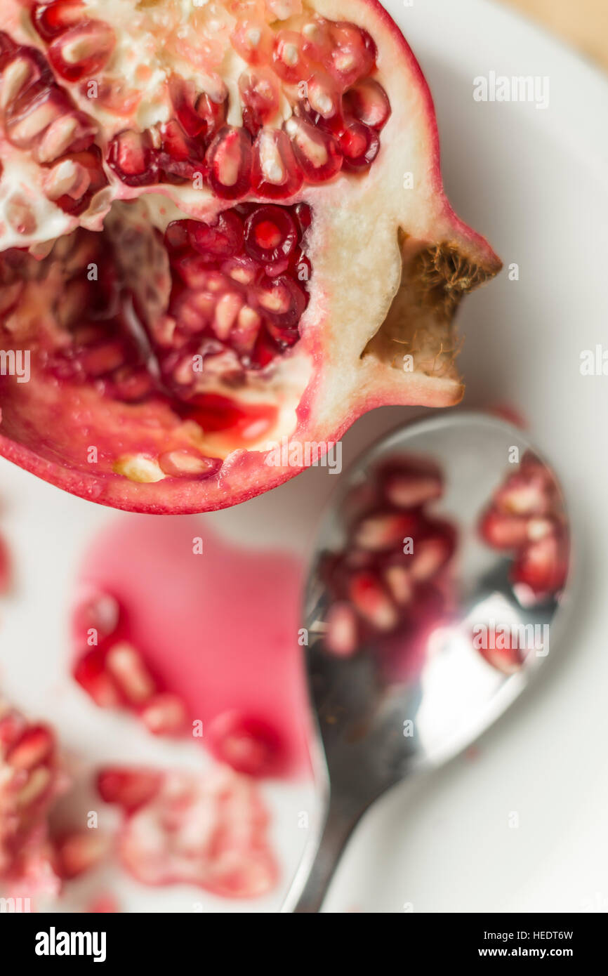 a large pomegranate sliced open, with seeds and juice with a spoon on a ...