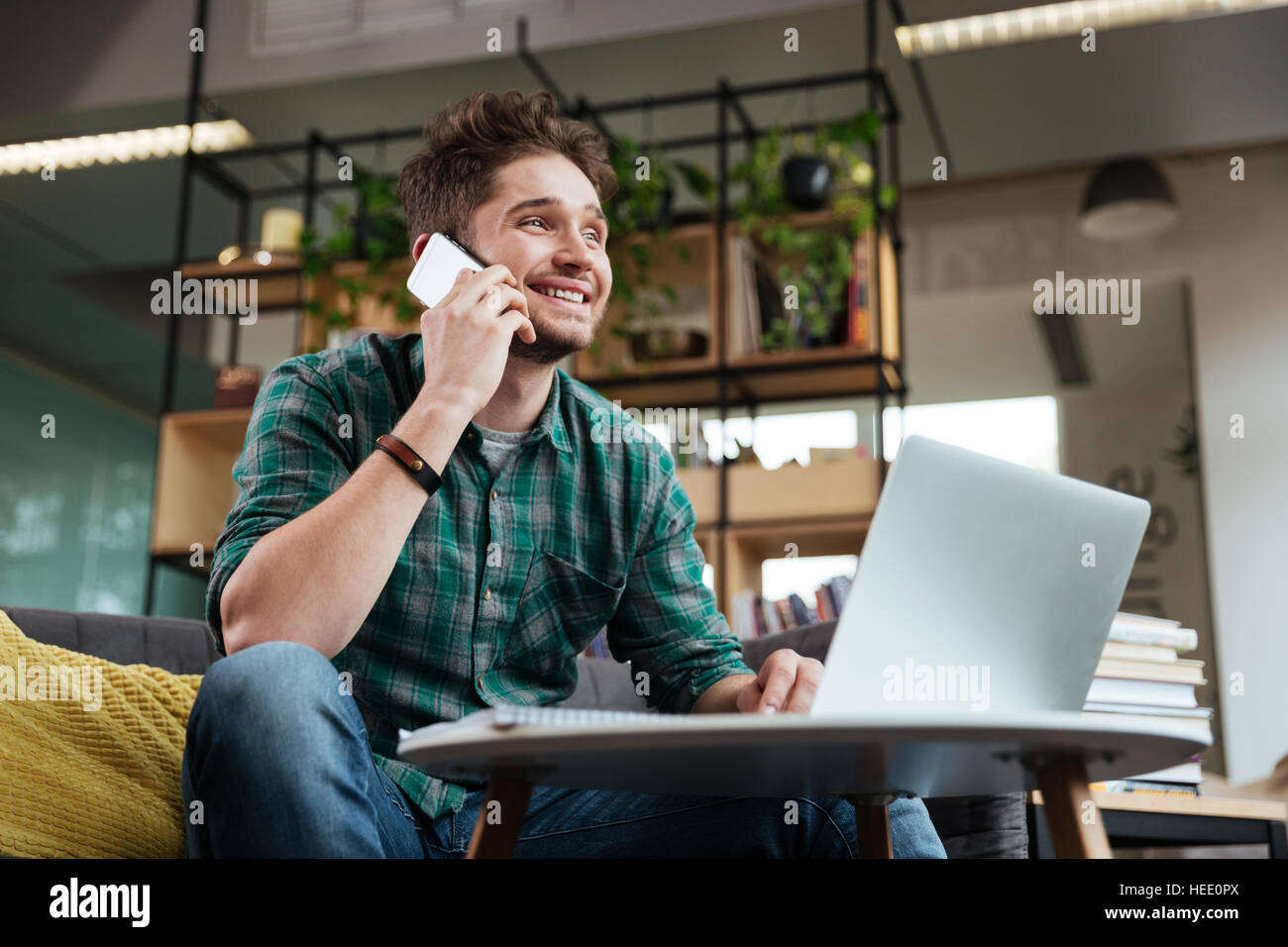 Happy man in green shirt sitting on sofa by the table with laptop and ...
