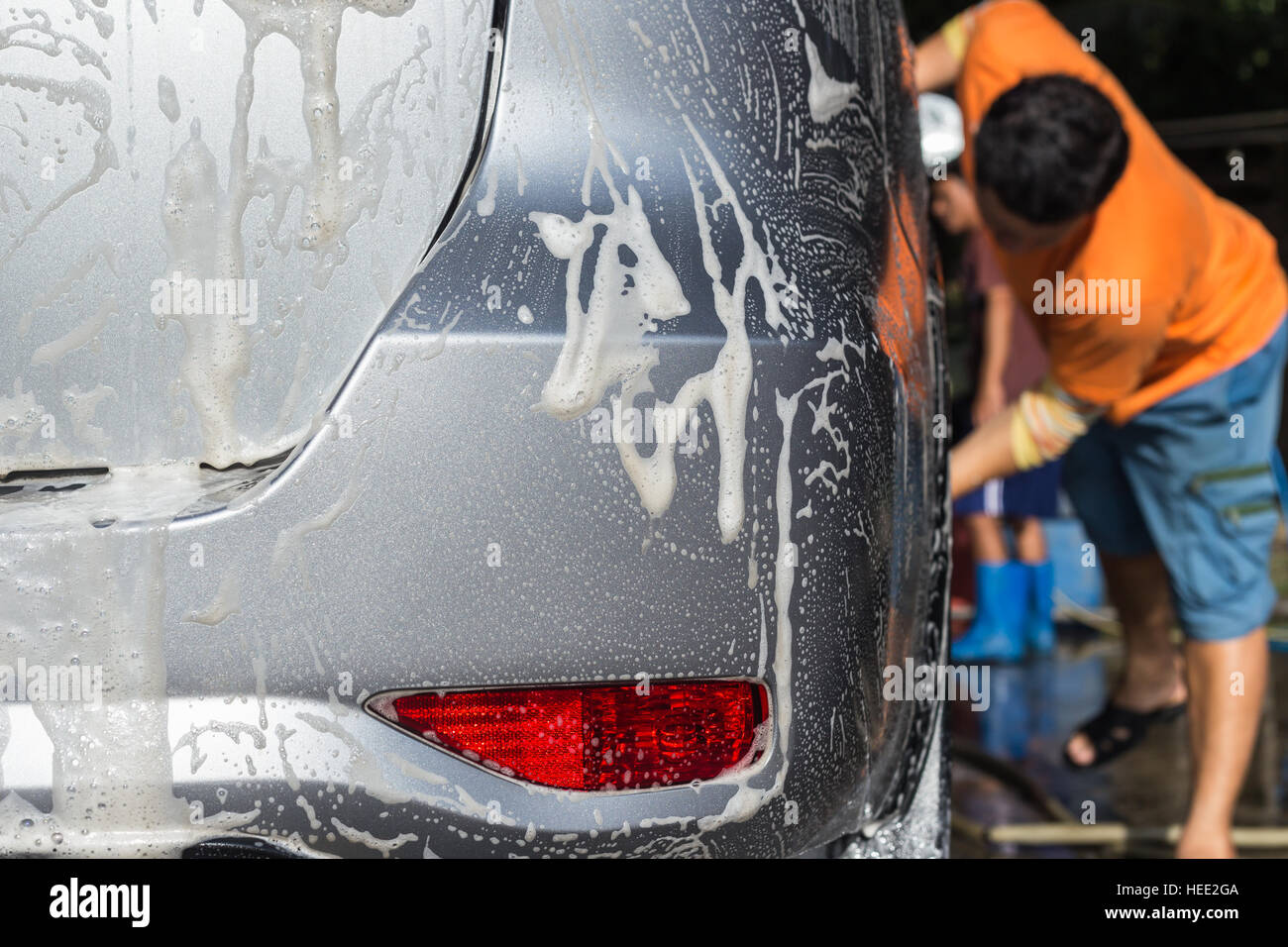 A man using soap for car washing in car care shop. Focus on backside of ...