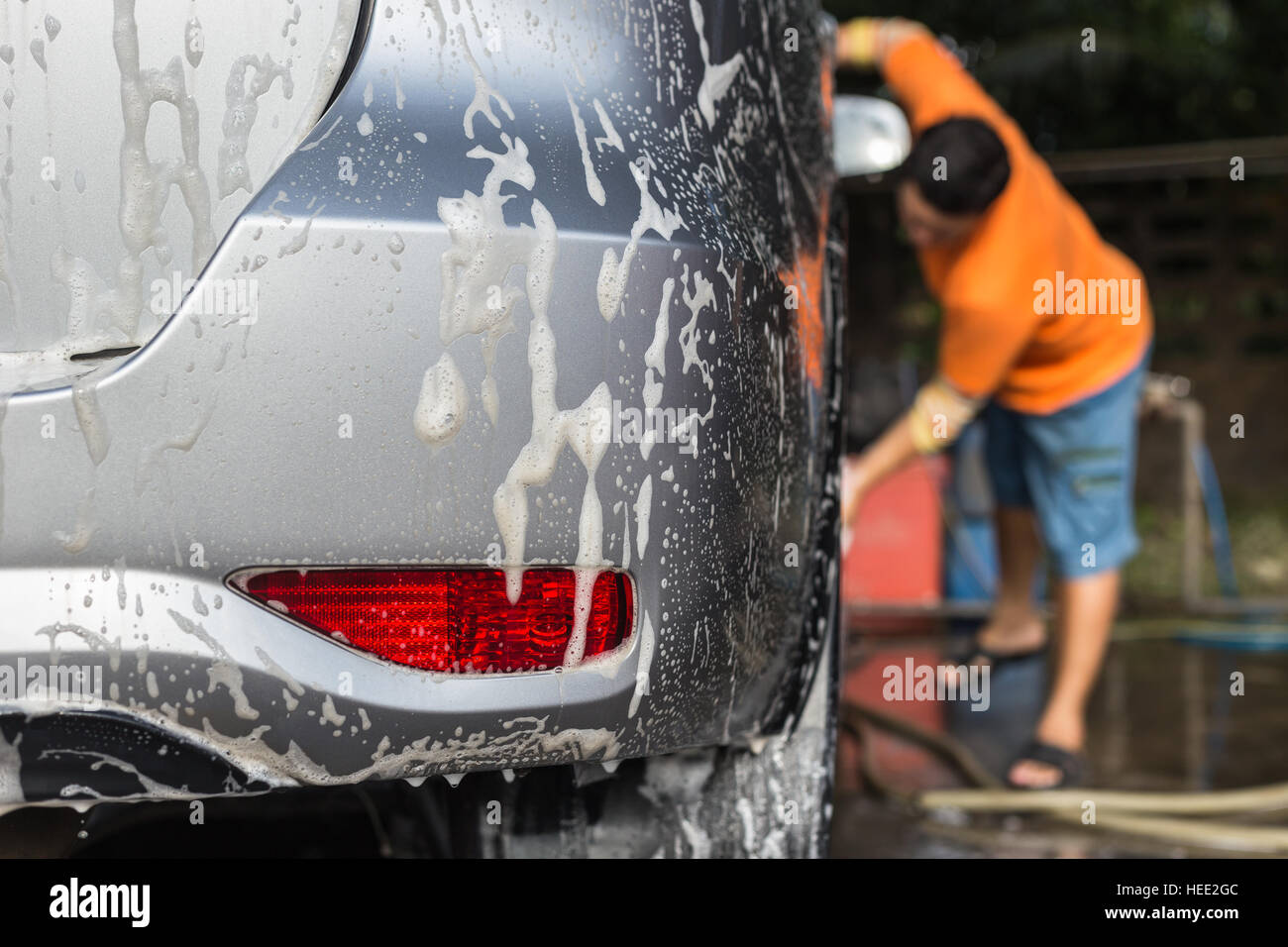 A man using soap for car washing in car care shop. Focus on backside of ...