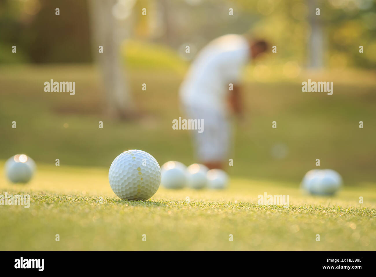 Close up golf ball and blurred of man playing golf in green course ...