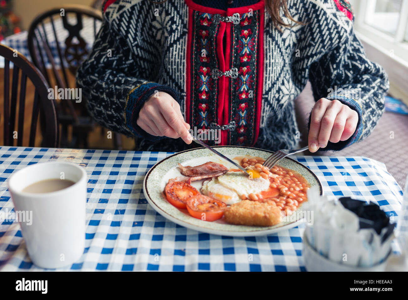 A young woman is having a traditional english breakfast with eggs ...