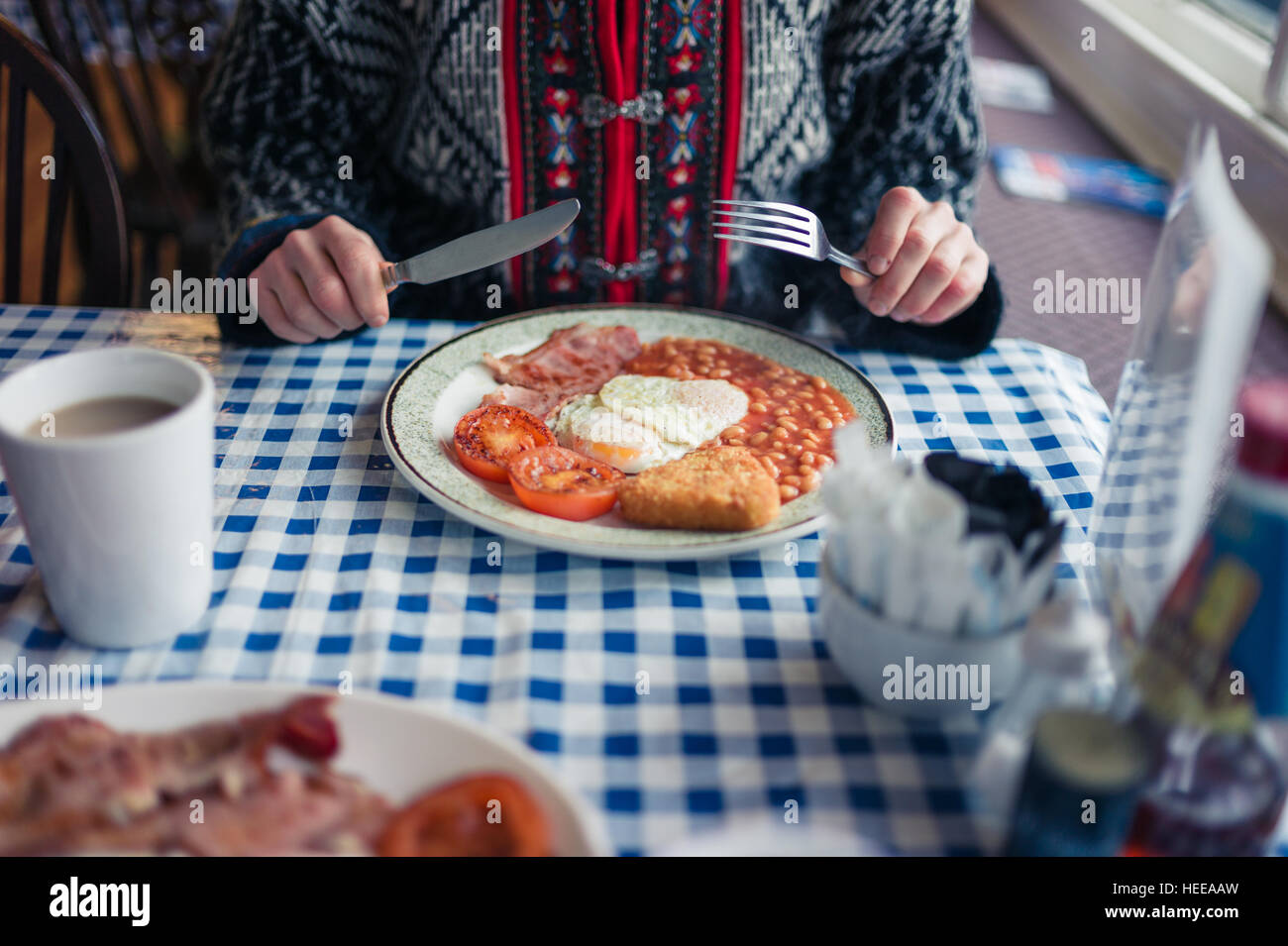 A young woman is having a traditional english breakfast with eggs ...