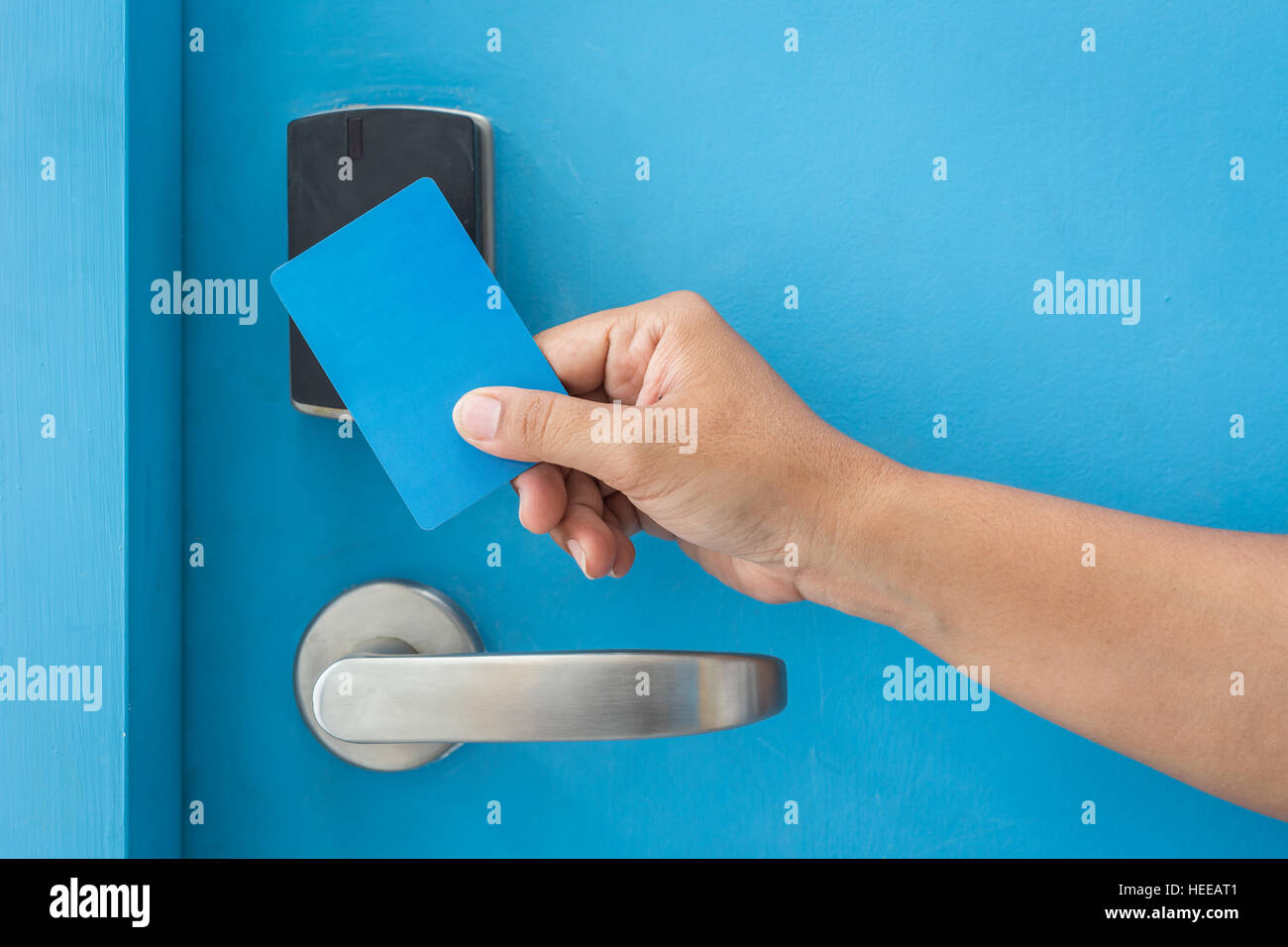 Close up hand holding blue hotel keycard in front of electric door ...