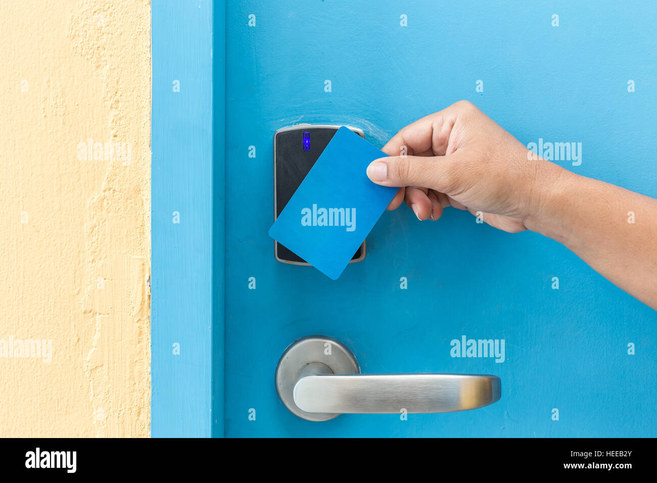 Close up hand holding blue hotel keycard in front of electric door ...