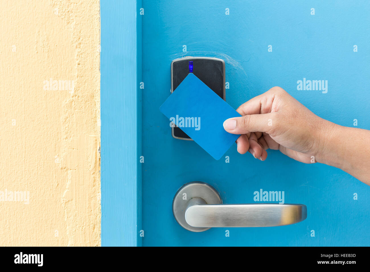 Close up hand holding blue hotel keycard in front of electric door ...