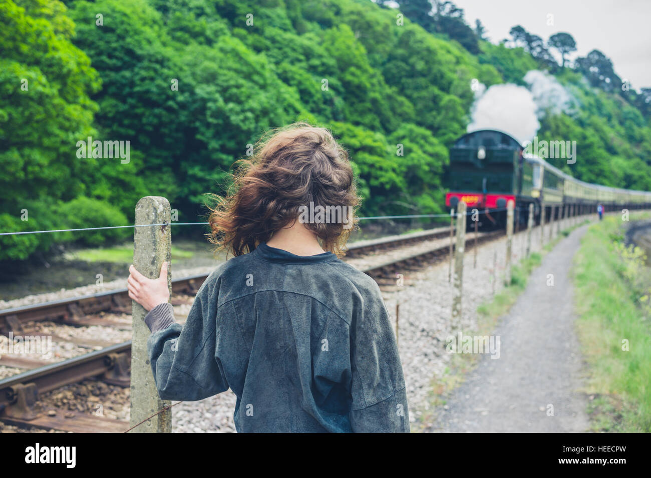 A young woman is standing by the railroad tracks and is watching an ...