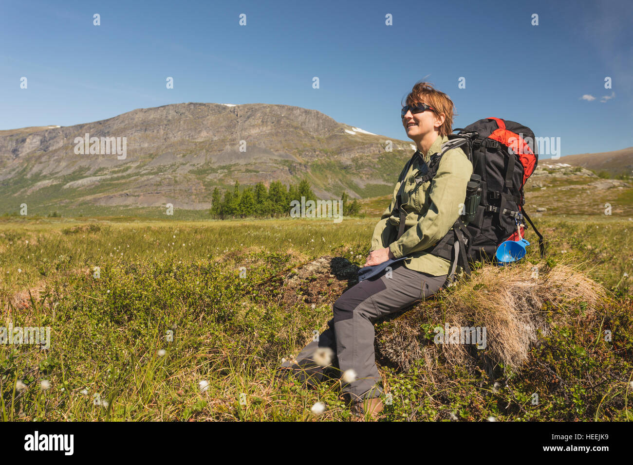 Woman hiking taking a rest, sitting down on a rock, mountain in the ...