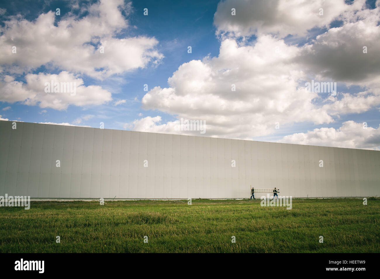 Two men carrying ladder along endless wall Stock Photo - Alamy
