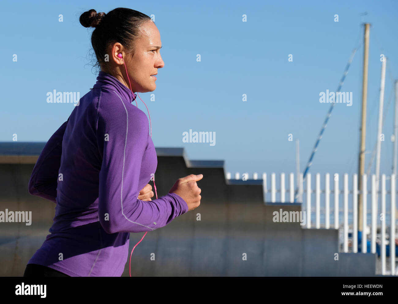 Young woman in purple shirt jogging in a sunny afternoon and listening ...