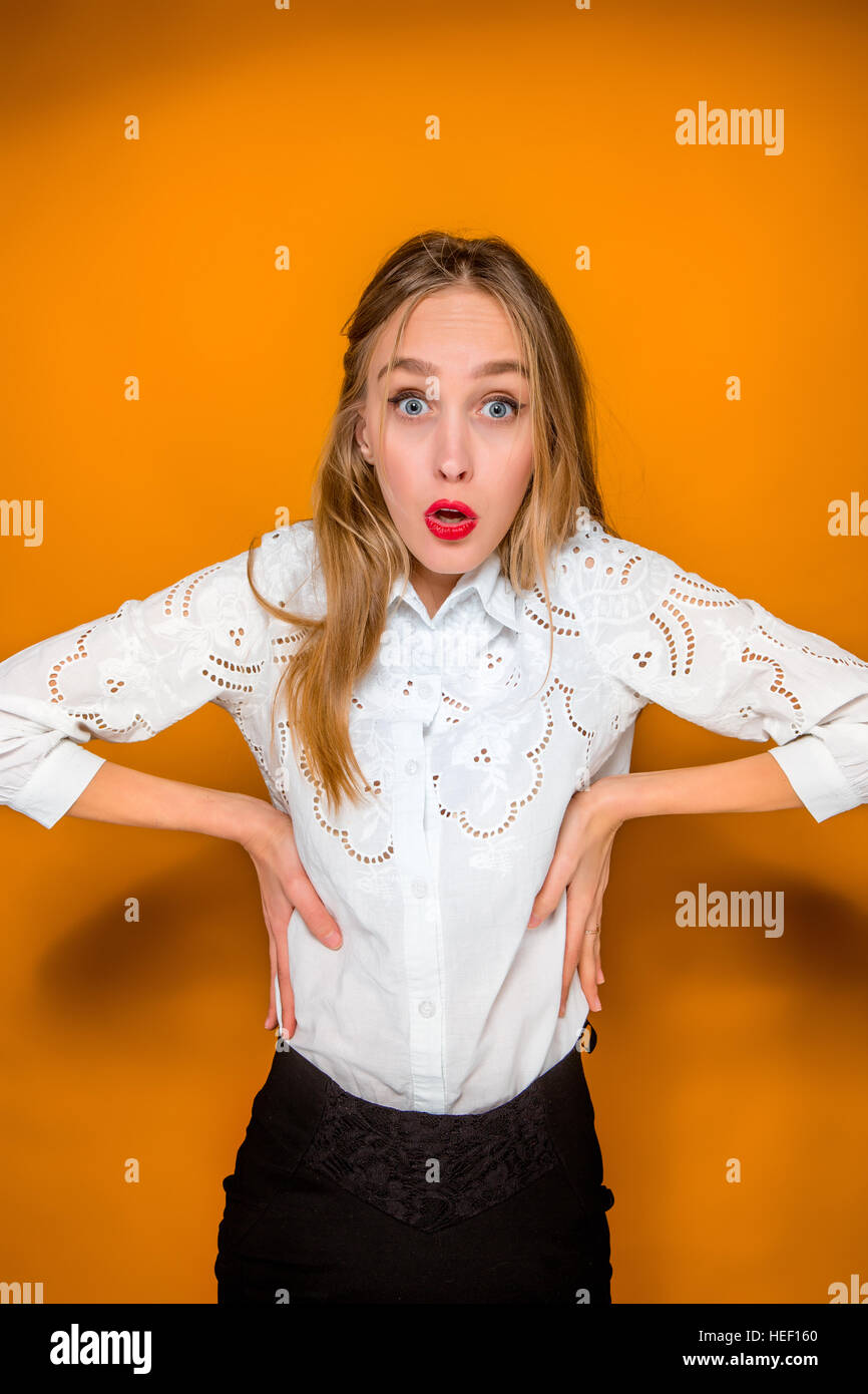 Portrait of young woman with shocked facial expression on orange studio ...