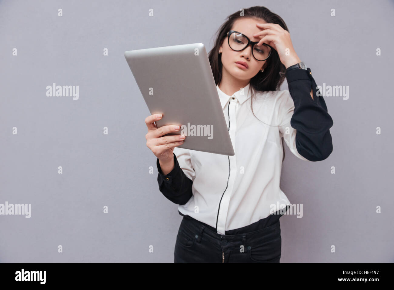 Pretty young Asian woman in glasses holding tablet computer. Focus on ...