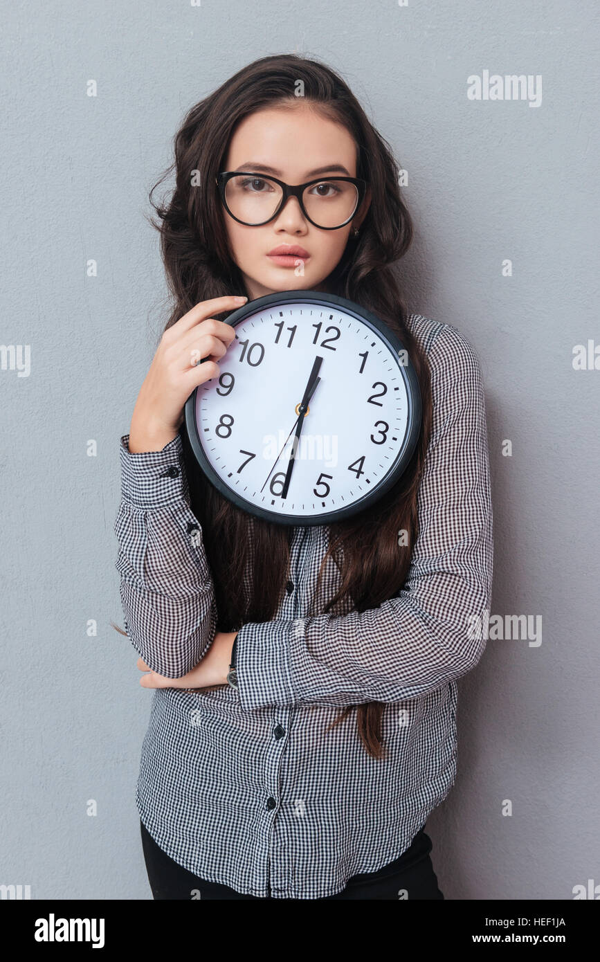 Vertical image of young cute asian woman in glasses holding clock and ...