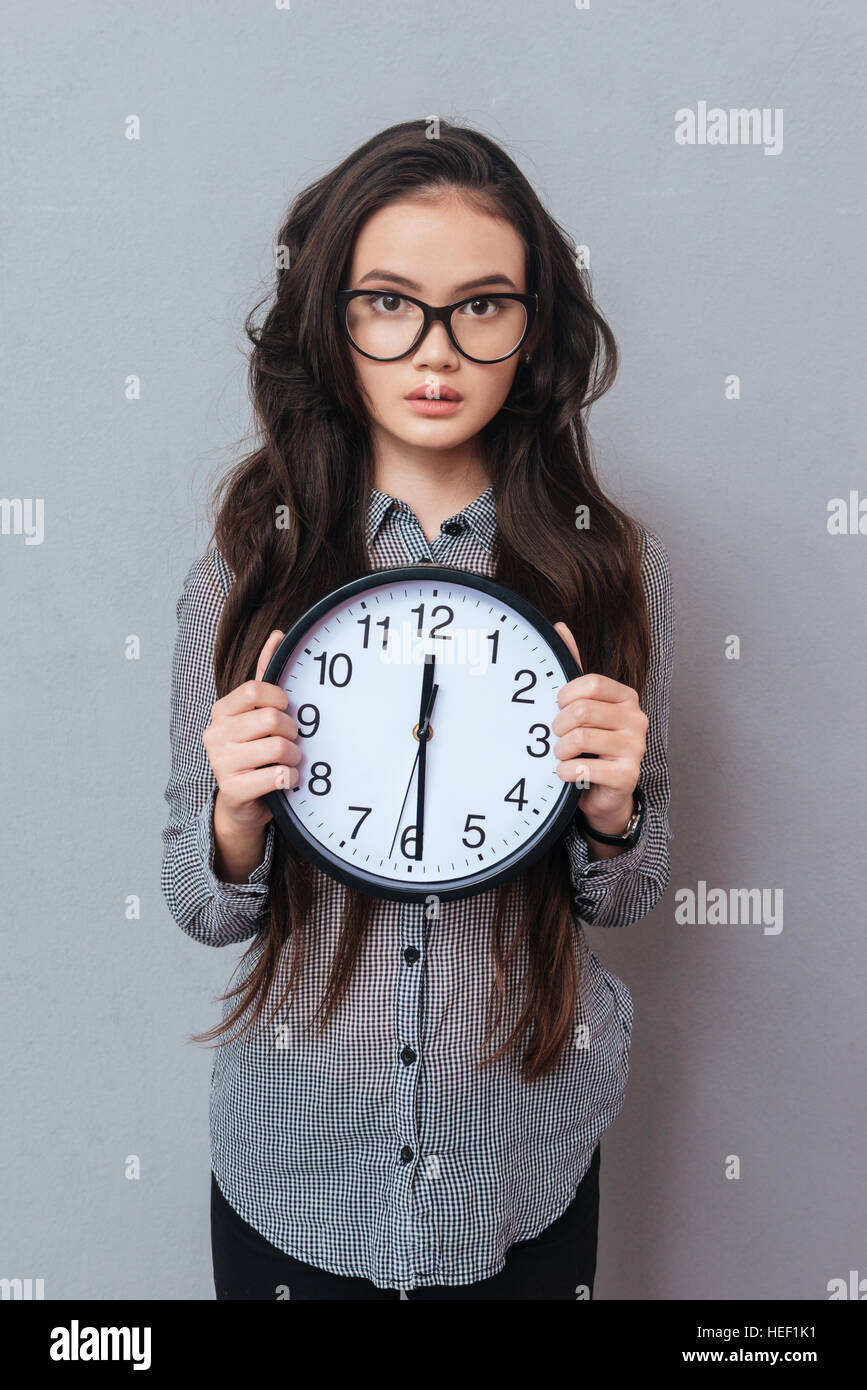 Vertical image of young serious asian woman holding clock in studio ...