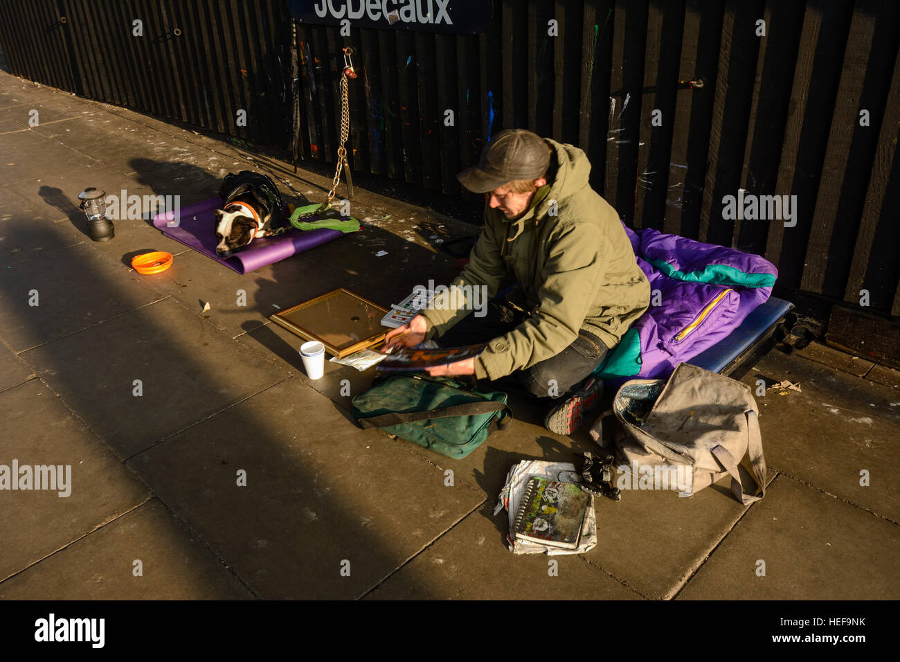 Homeless young man living on the streets of Manchester sat painting a ...