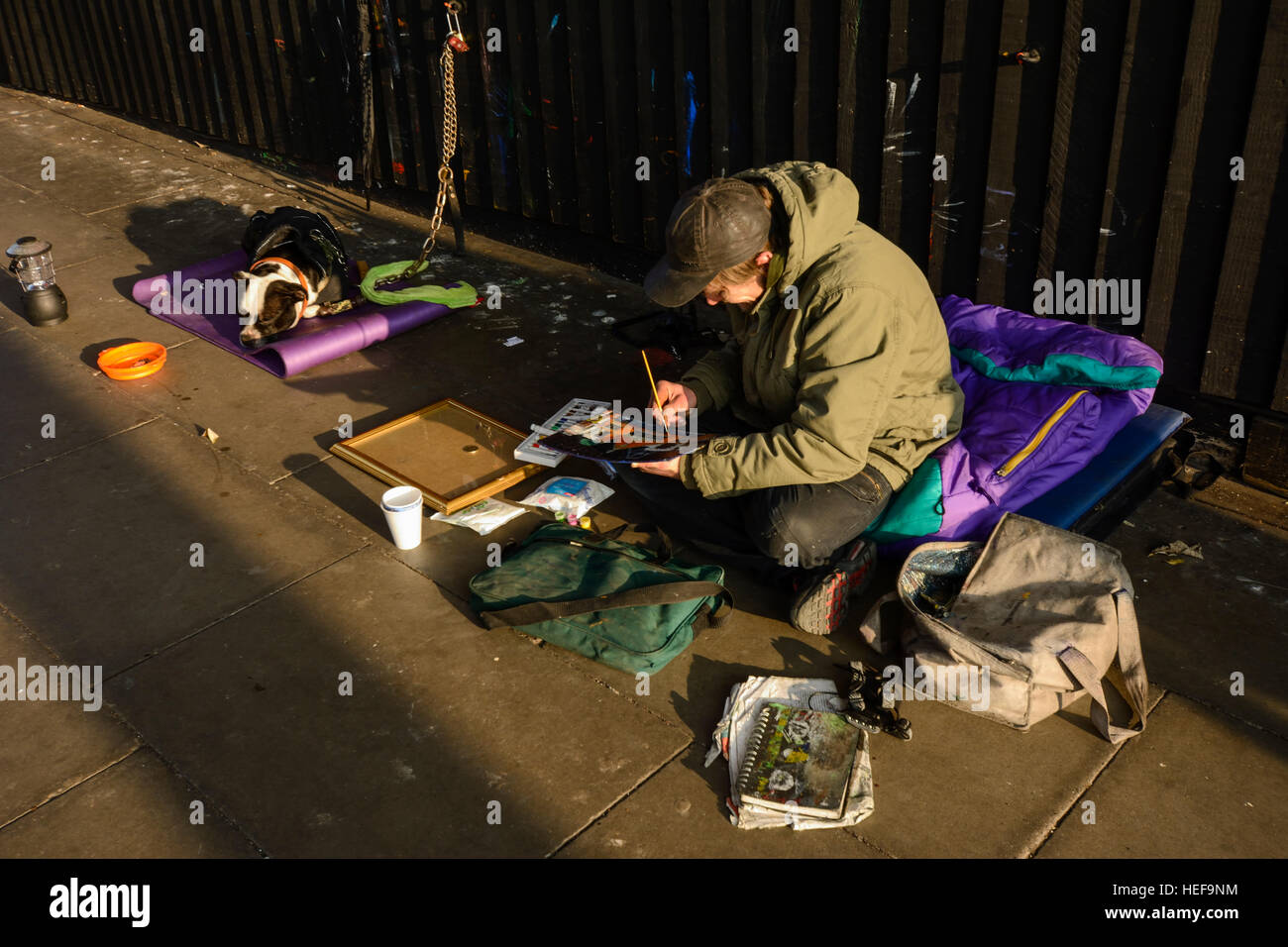 Homeless young man living on the streets of Manchester sat painting a ...