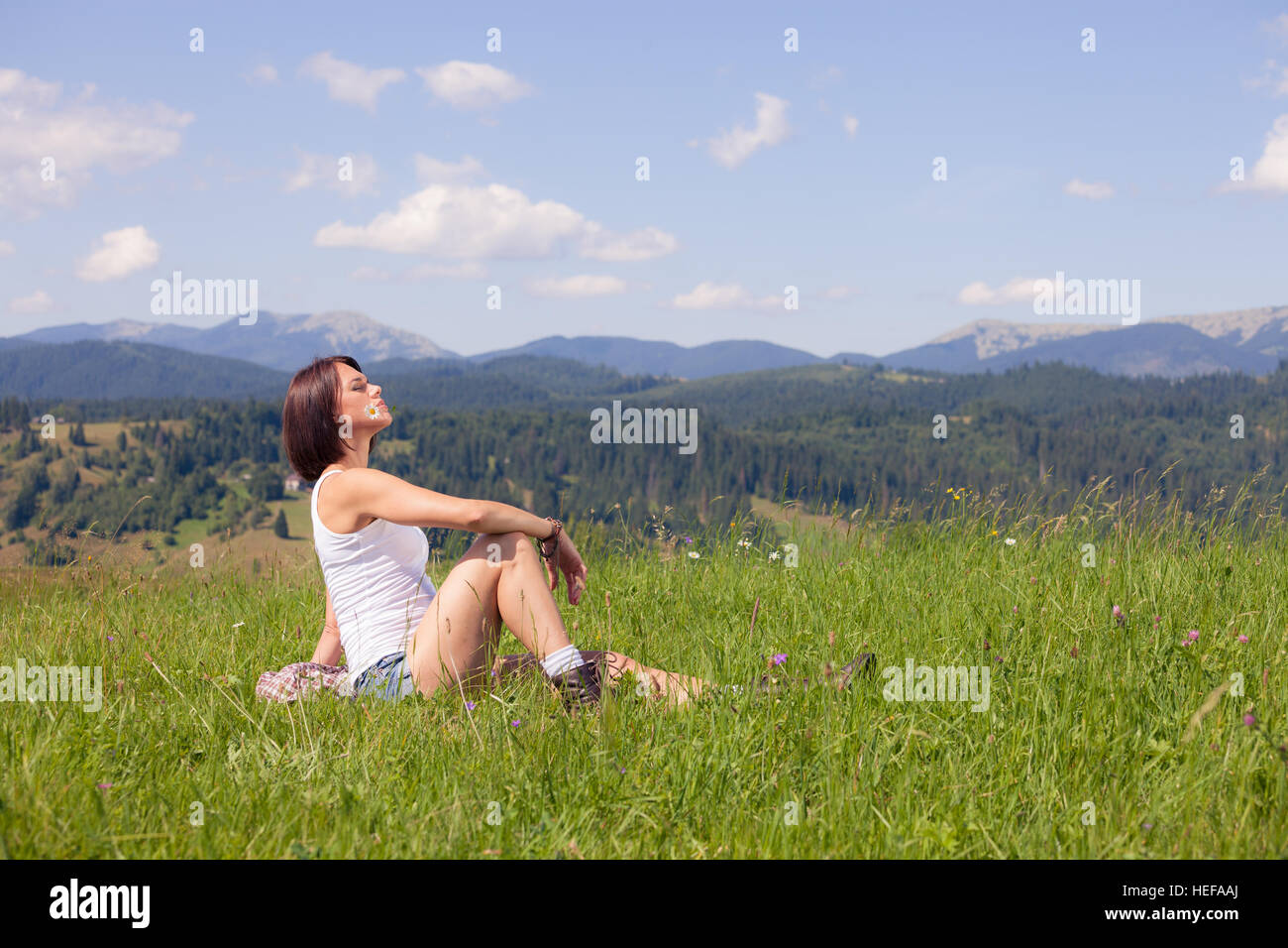 Beautiful girl lying on green grass field and holding flower in her ...
