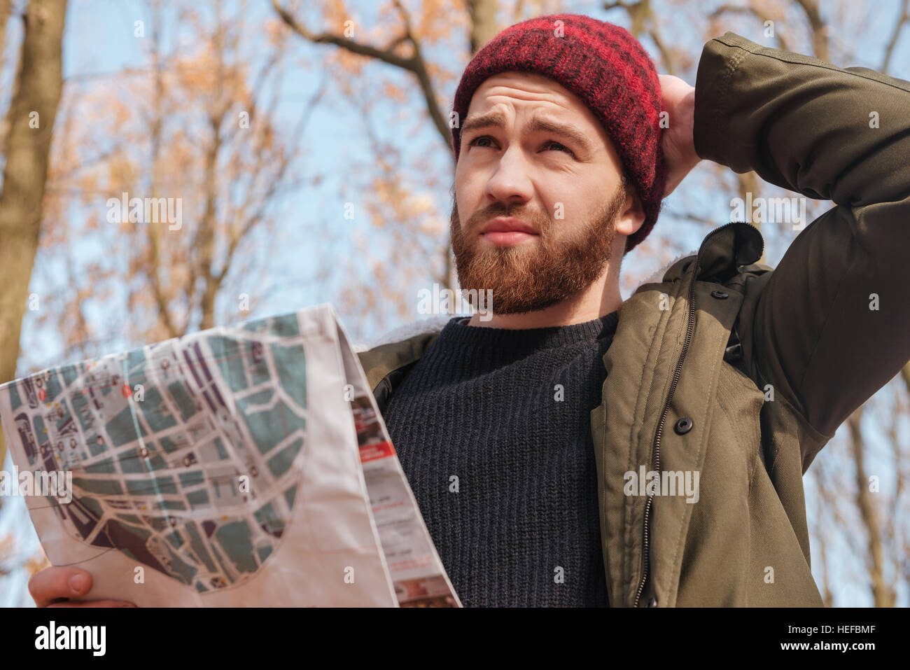 Portrait of confused bearded man wearing hat holding map in hands ...