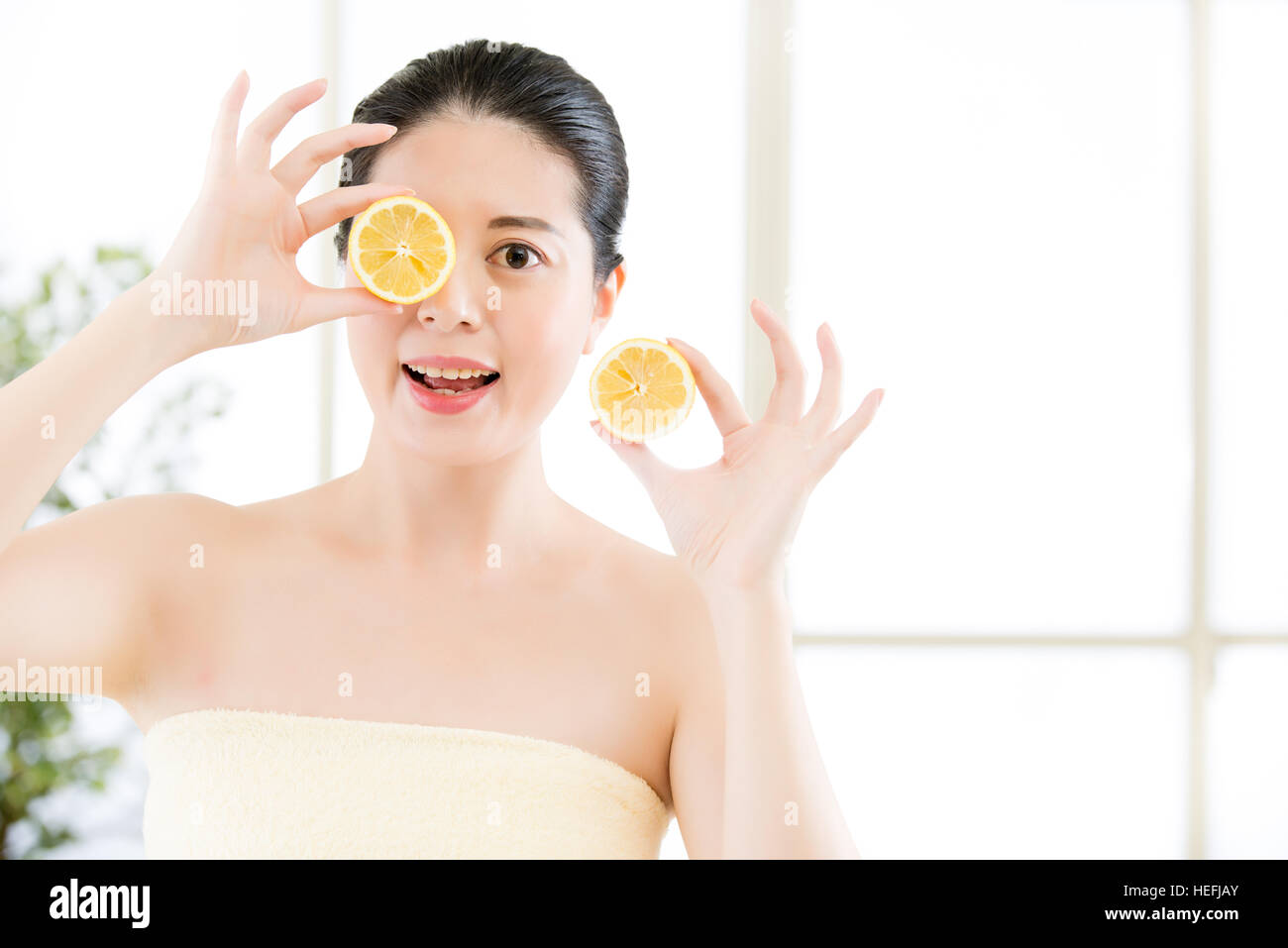 Woman with clean face holding slices of lemon over eyes. Lemon for ...