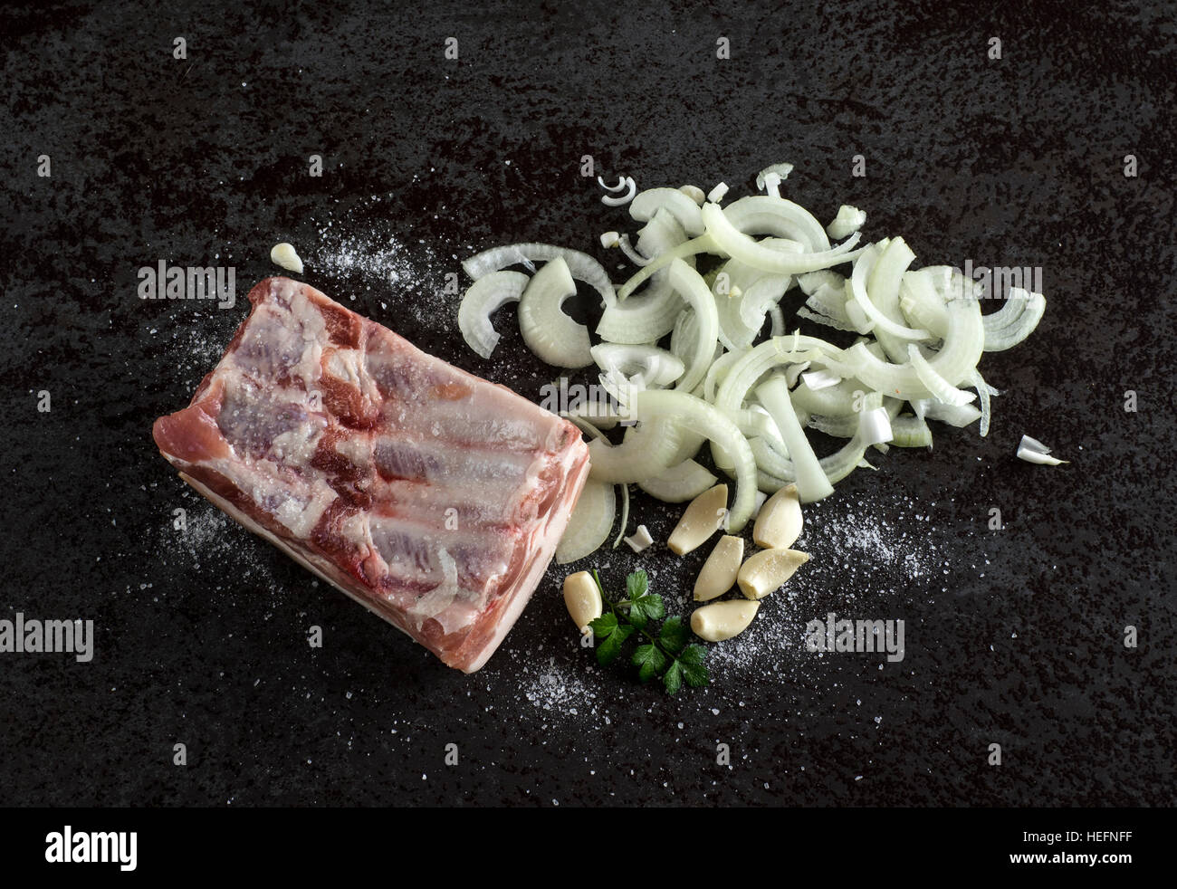 Raw pork brisket, garlic and chopped for half rings onion on a dark ...