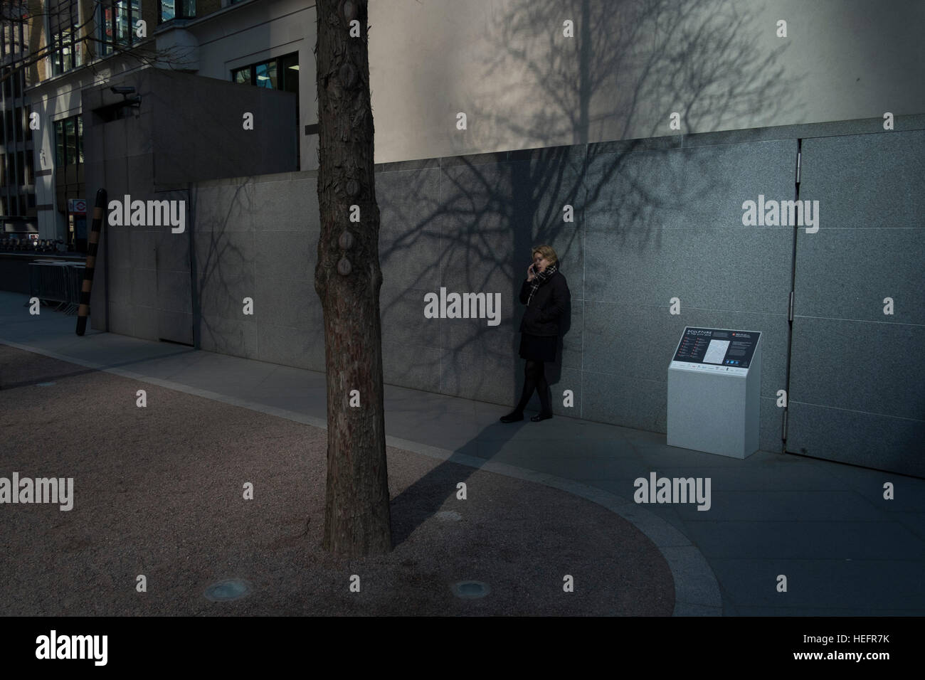 Woman on her cell phone beside a wall with a tree shadow within street ...